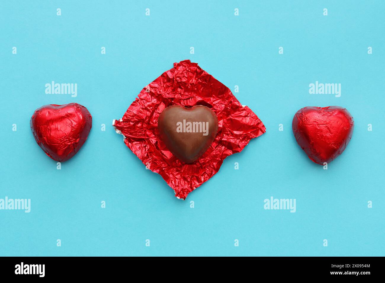 Three red heart-shaped candies on a blue paper background, top view.Two ...