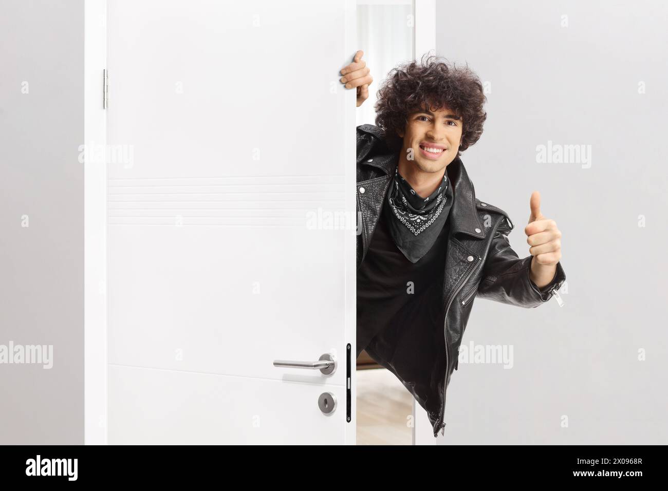 Guy in a black leather jacket behind a door gesturing thumbs up and ...