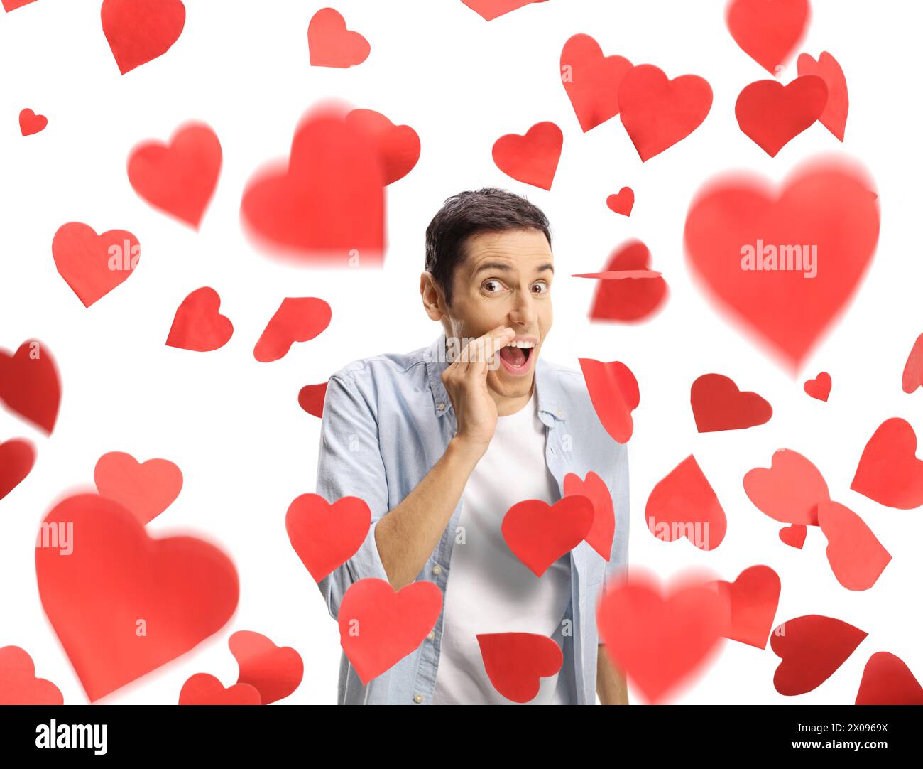 Excited young man whispering under red falling hearts isolated on white ...