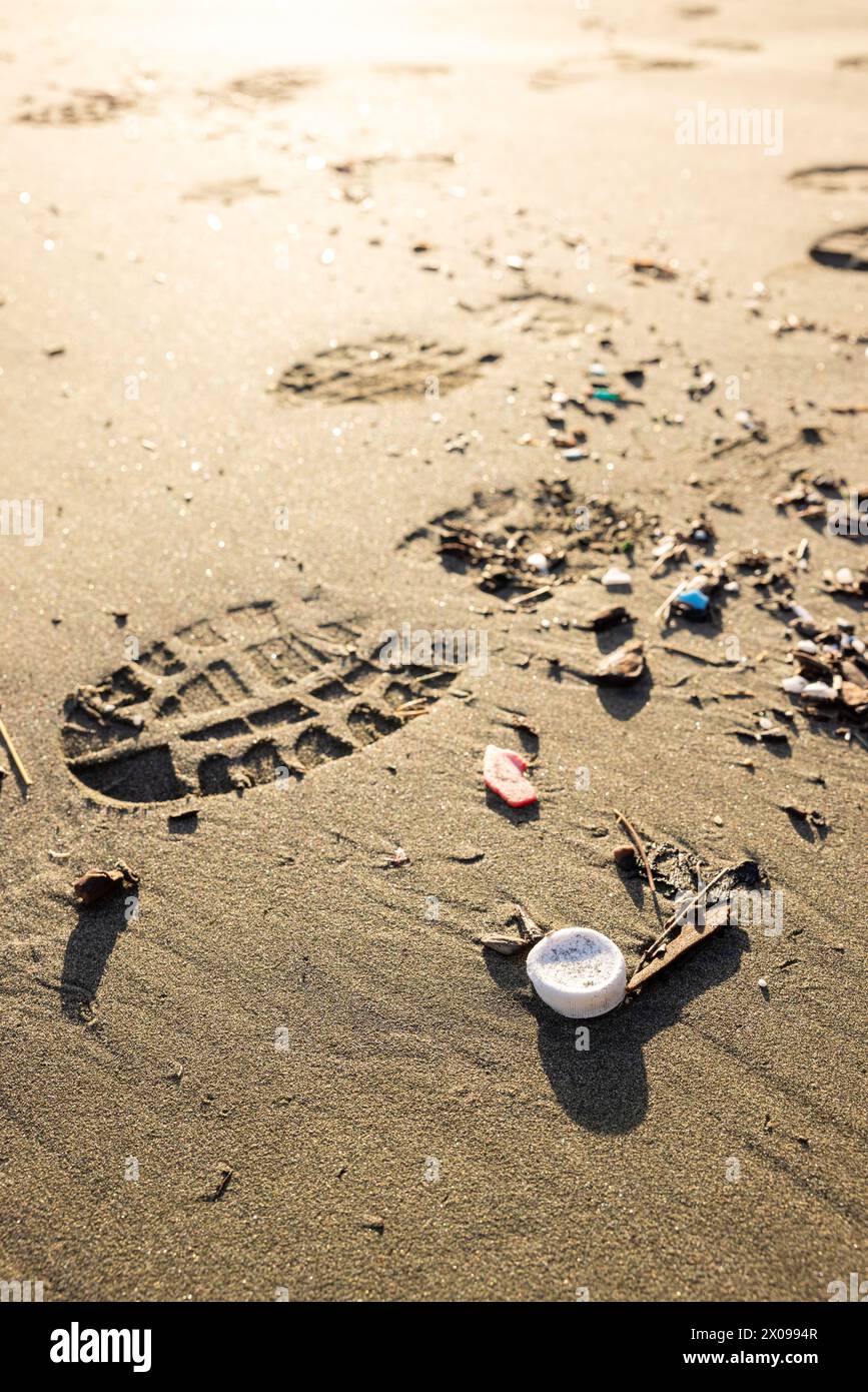 A beach with trash on the sand and a footprint in the sand. Scene is ...