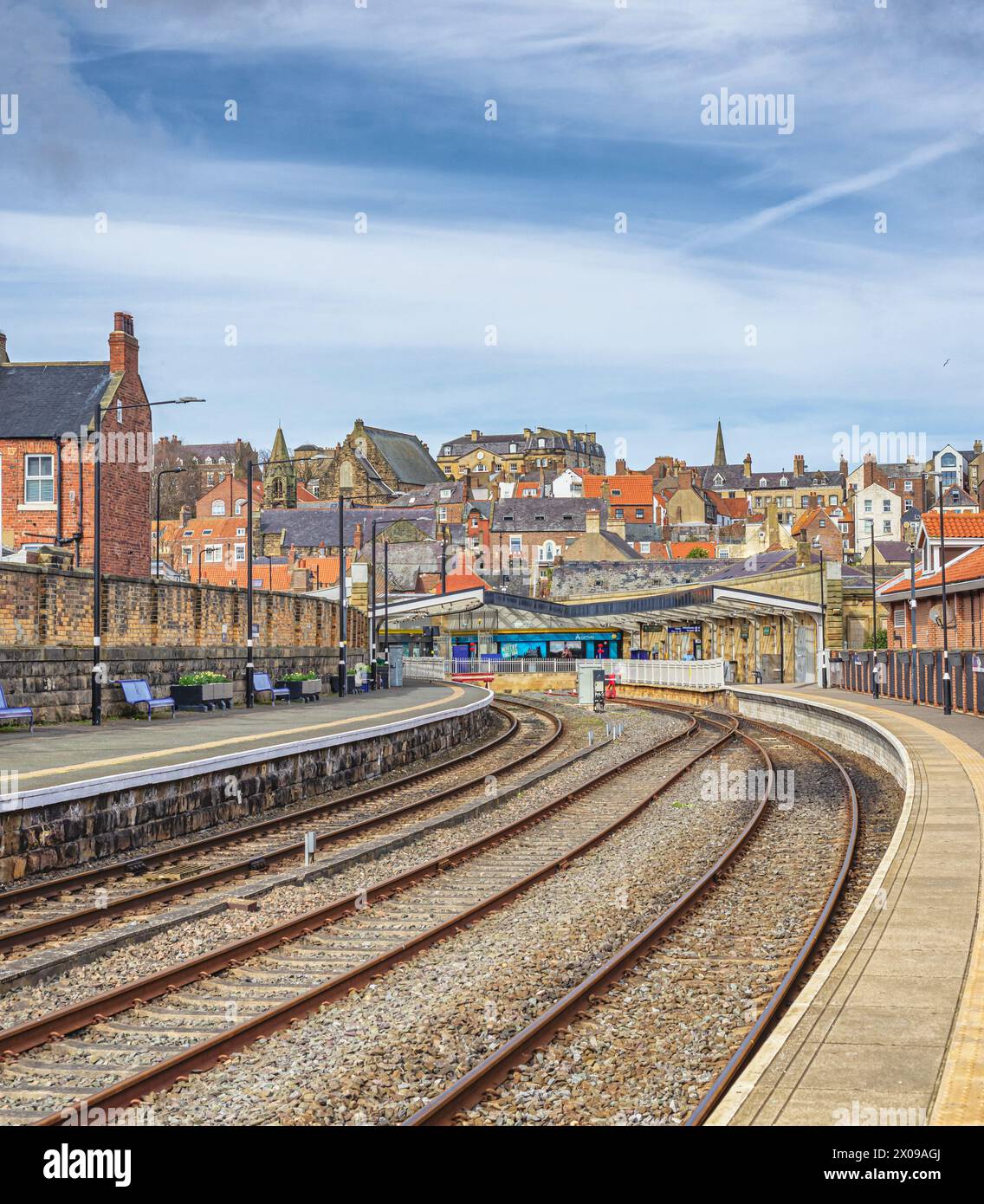 Railway tracks curve into a railway station terminus. Benches and ...
