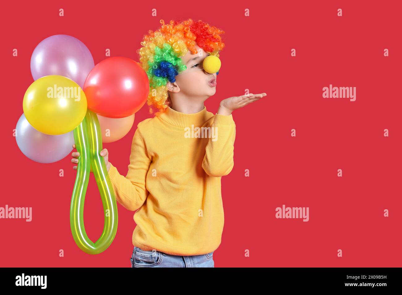 Funny little boy in clown costume with balloons blowing kiss on red ...