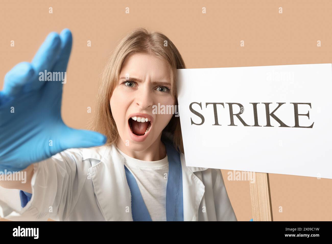 Protesting female doctor holding placard with text STRIKE on beige ...
