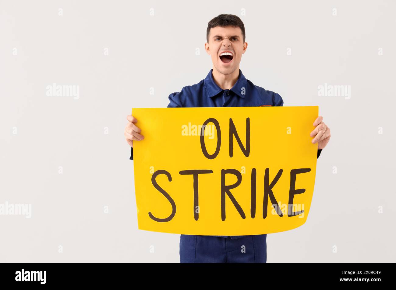 Protesting mechanic holding placard with text ON STRIKE against light ...