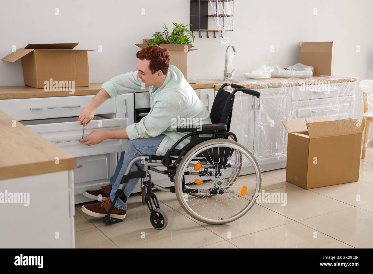 Young man in wheelchair repairing kitchen drawer at home Stock Photo ...