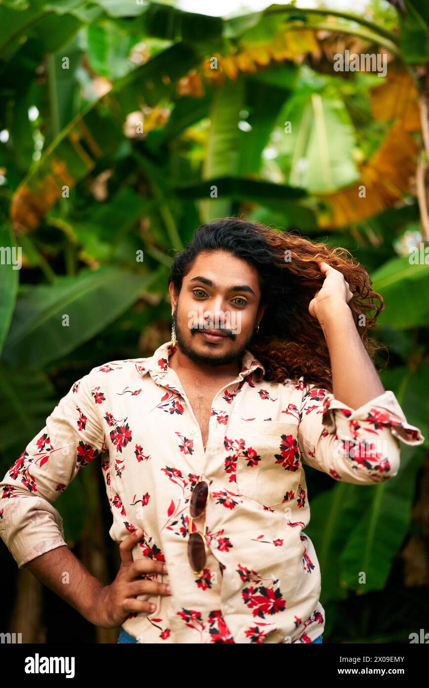 Vibrant man with rich curly hair, floral shirt stands in tropical green ...