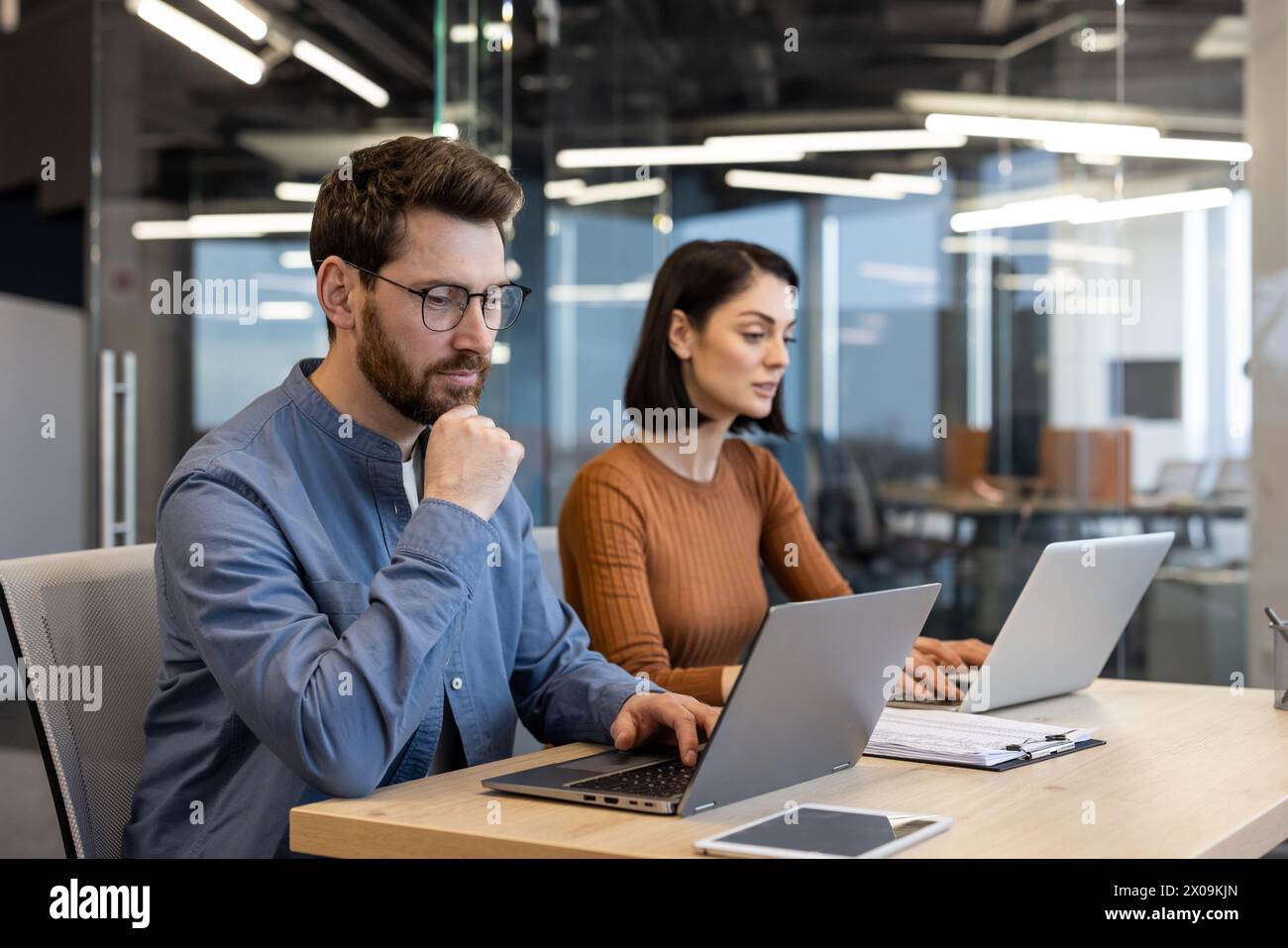 Two focused professionals working together at a desk with laptops in a ...