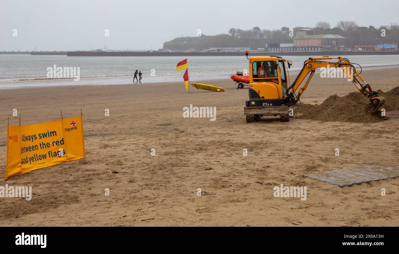 Mini digger piling the sand up on the beach at Weymouth Dorset UK on a ...