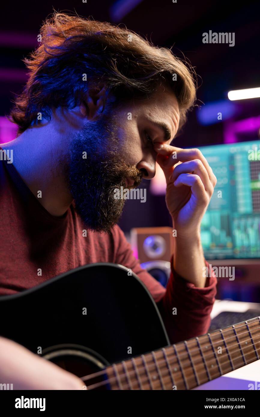 Stressed sleepy artist practicing acoustic instrument in his home ...