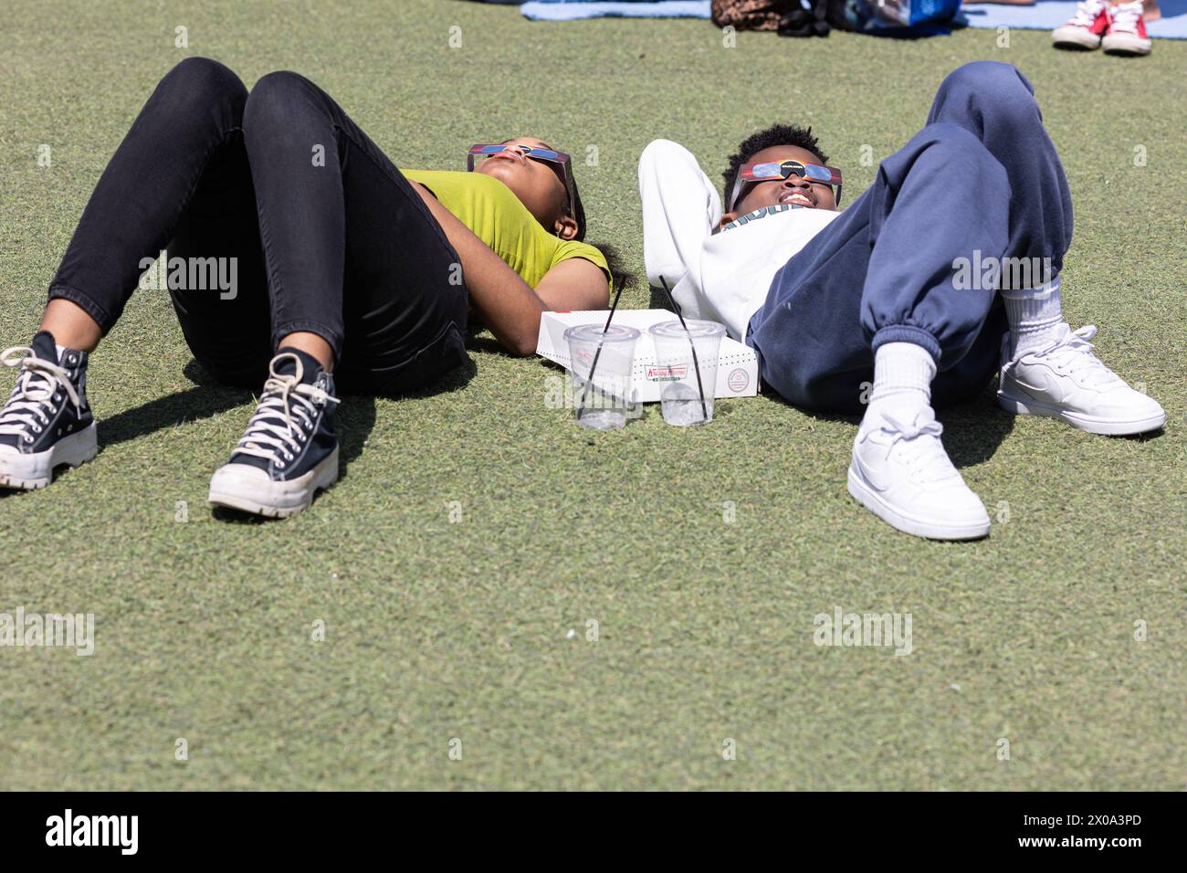 Atlanta, GA / USA - April 8, 2024: Two teens lie on the ground and look ...