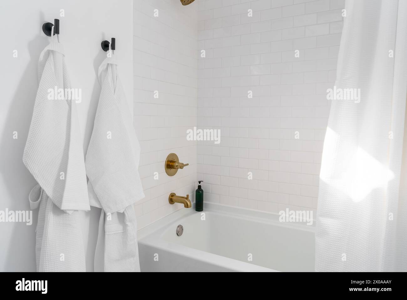 white home bathroom shower tub with brass hardware and bath robes ...