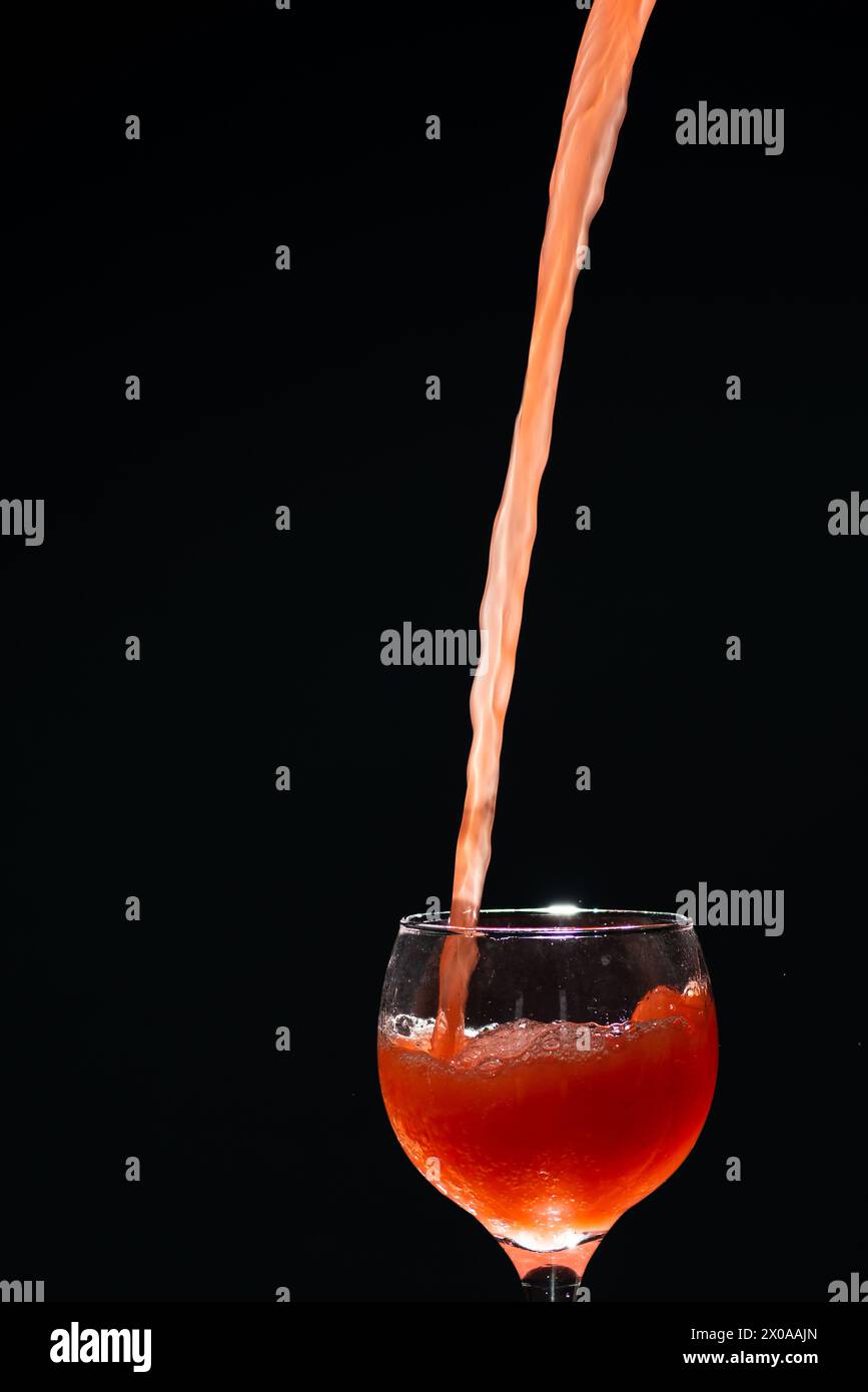 Guava juice falling into a glass cup held by a hand. Isolated on dark ...