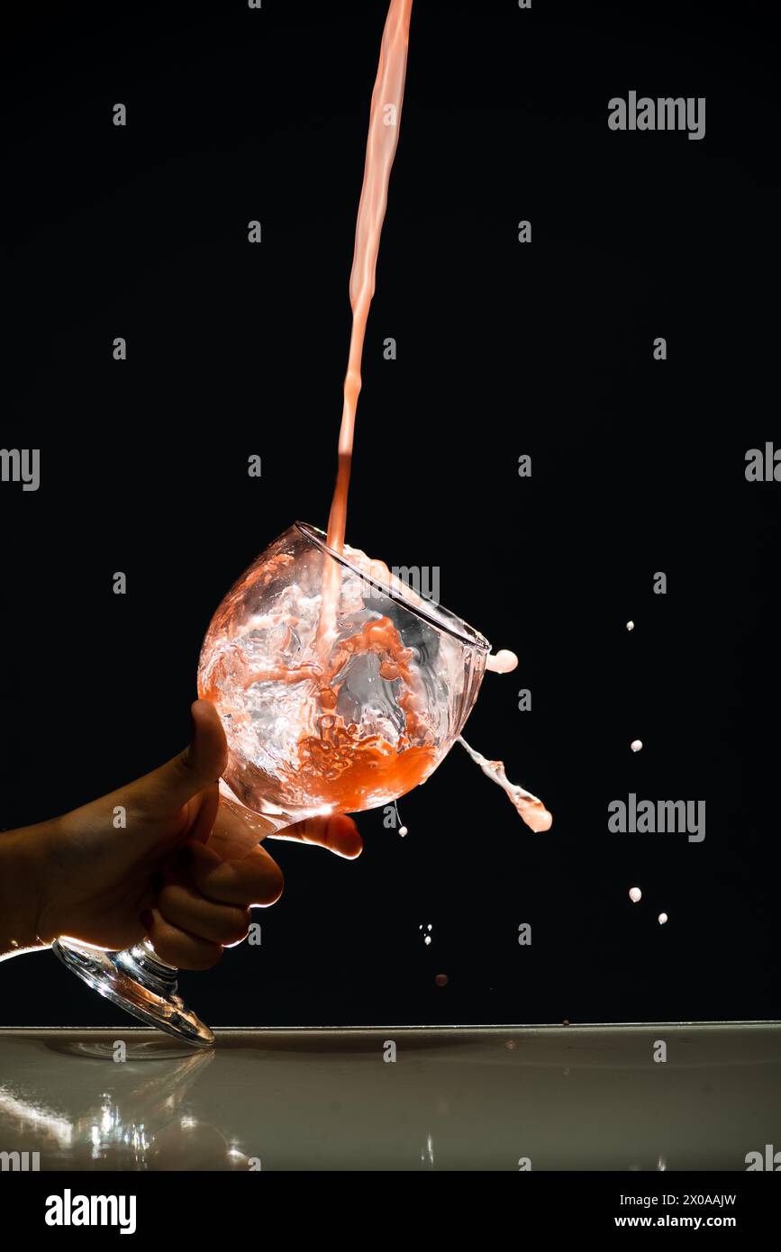 Guava juice falling from a plastic container into a glass cup held by a ...