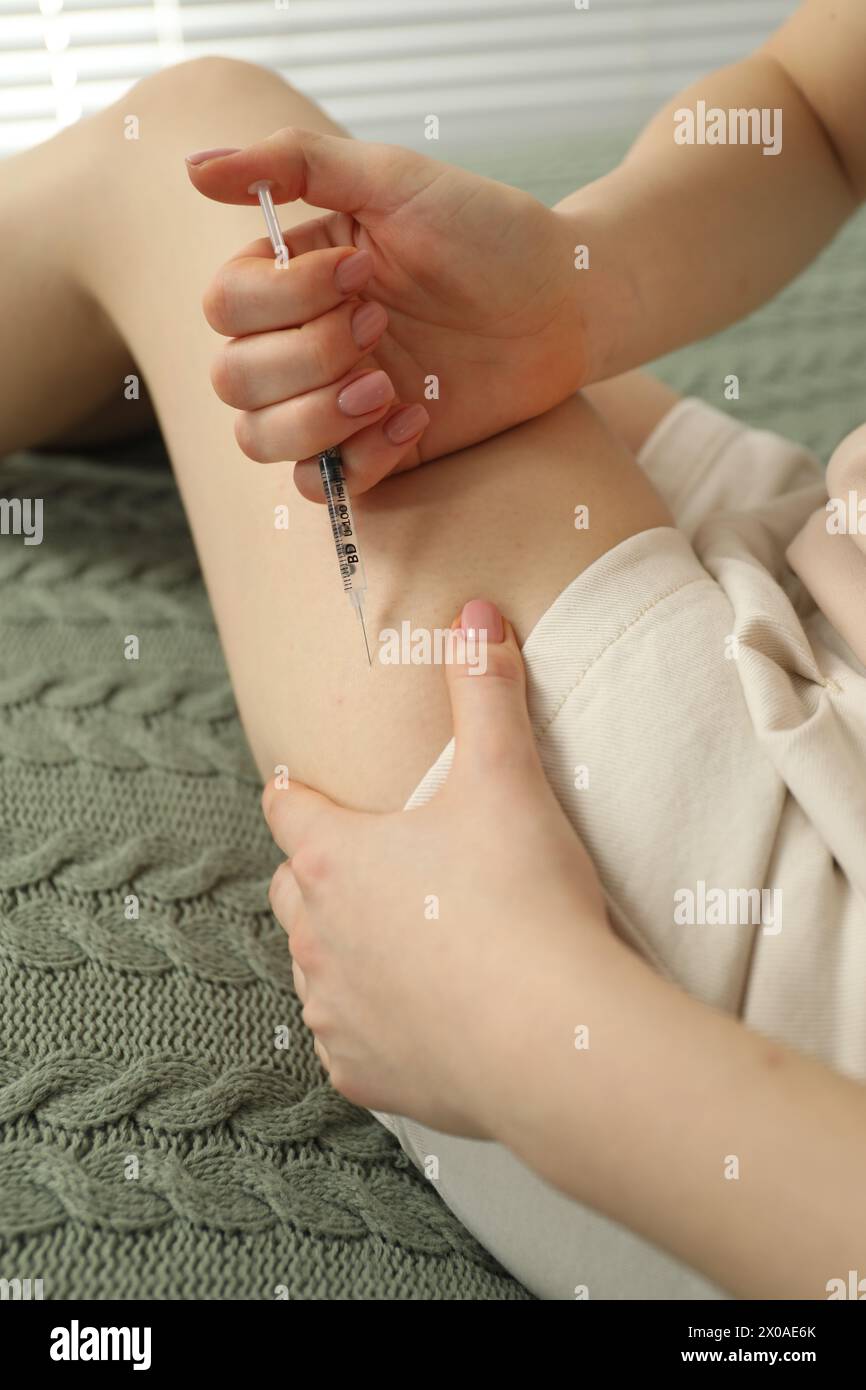 Diabetes. Woman making insulin injection into her leg on bed indoors ...