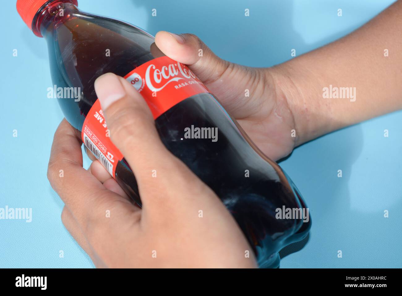 Close up view of a hand holding a Coca Cola product. Against a blue ...