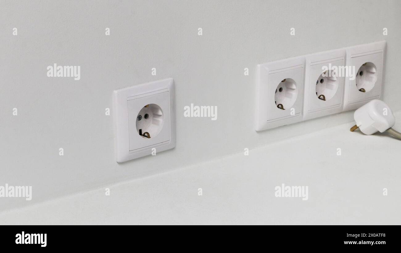 Four electrical sockets on a light wall and one electrical plug with a ...