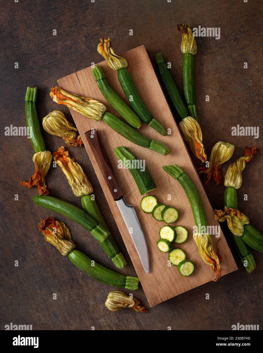 Overhead view of fresh picked zucchini with blooms on a brown surface ...