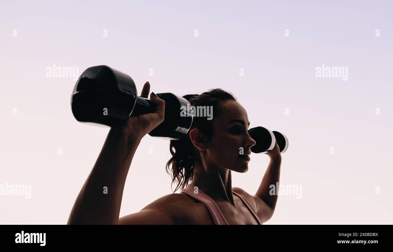 Silhouetted woman engaging in upper body strength training with ...