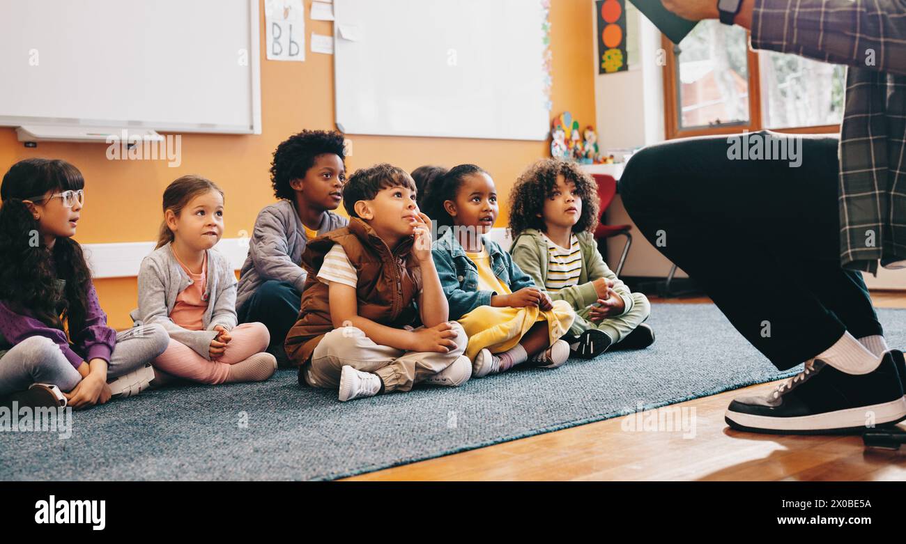 Elementary school students sit and listen to a story from their teacher ...