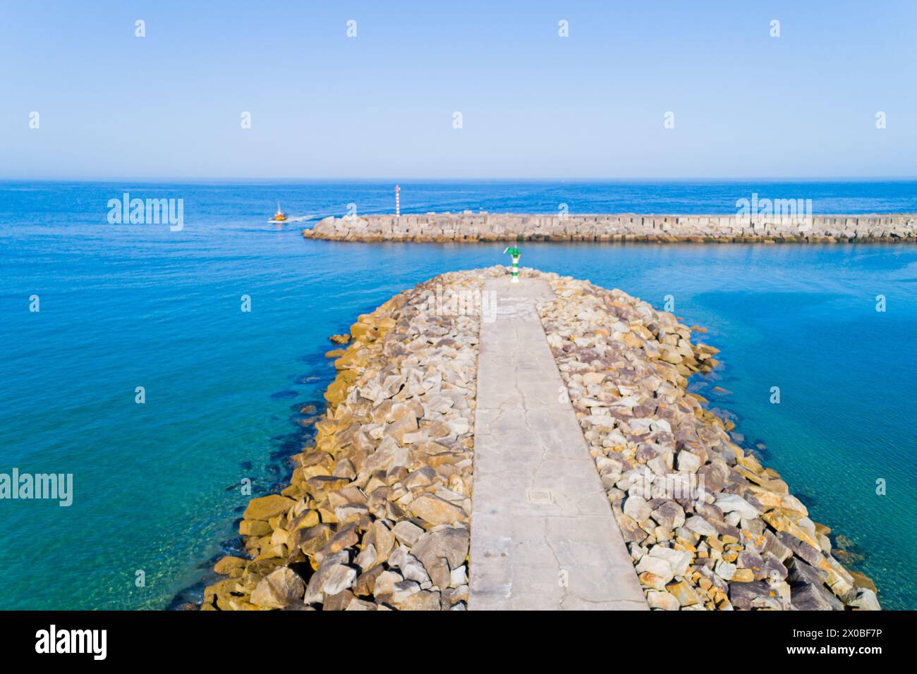 photo of a breakwater at the entrance of a harbor and a ship arriving ...