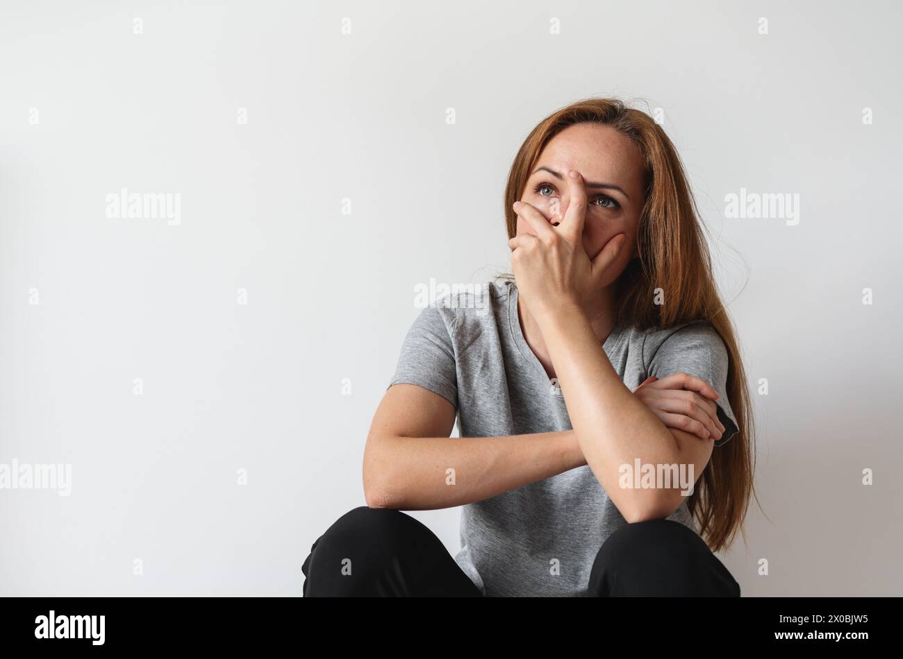 Unhappy depressed woman sits next to grey wall covers face with her ...