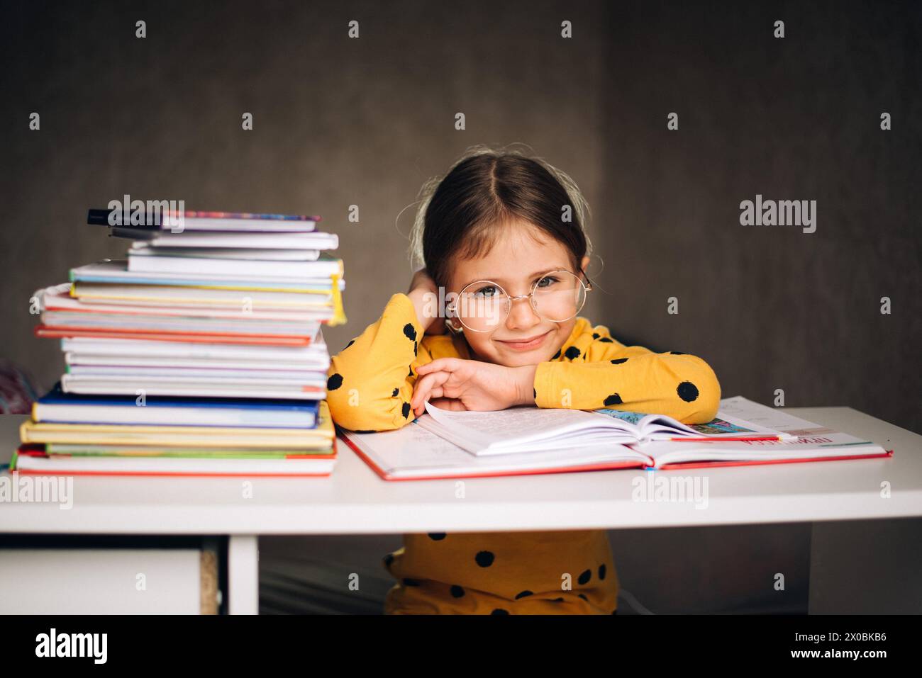 a girl with round glasses reading a book at a table near a stack of ...