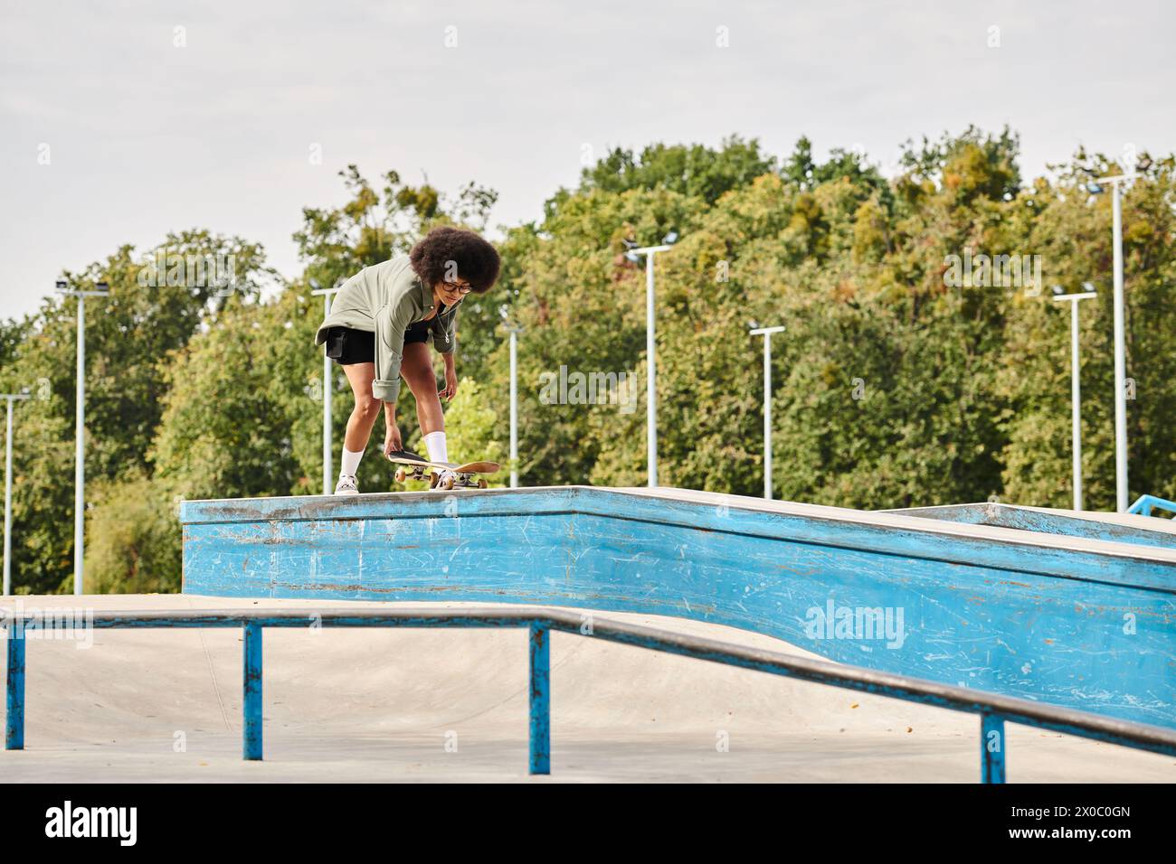 A woman with a skateboard rides down a steep ramp in an outdoor skate ...