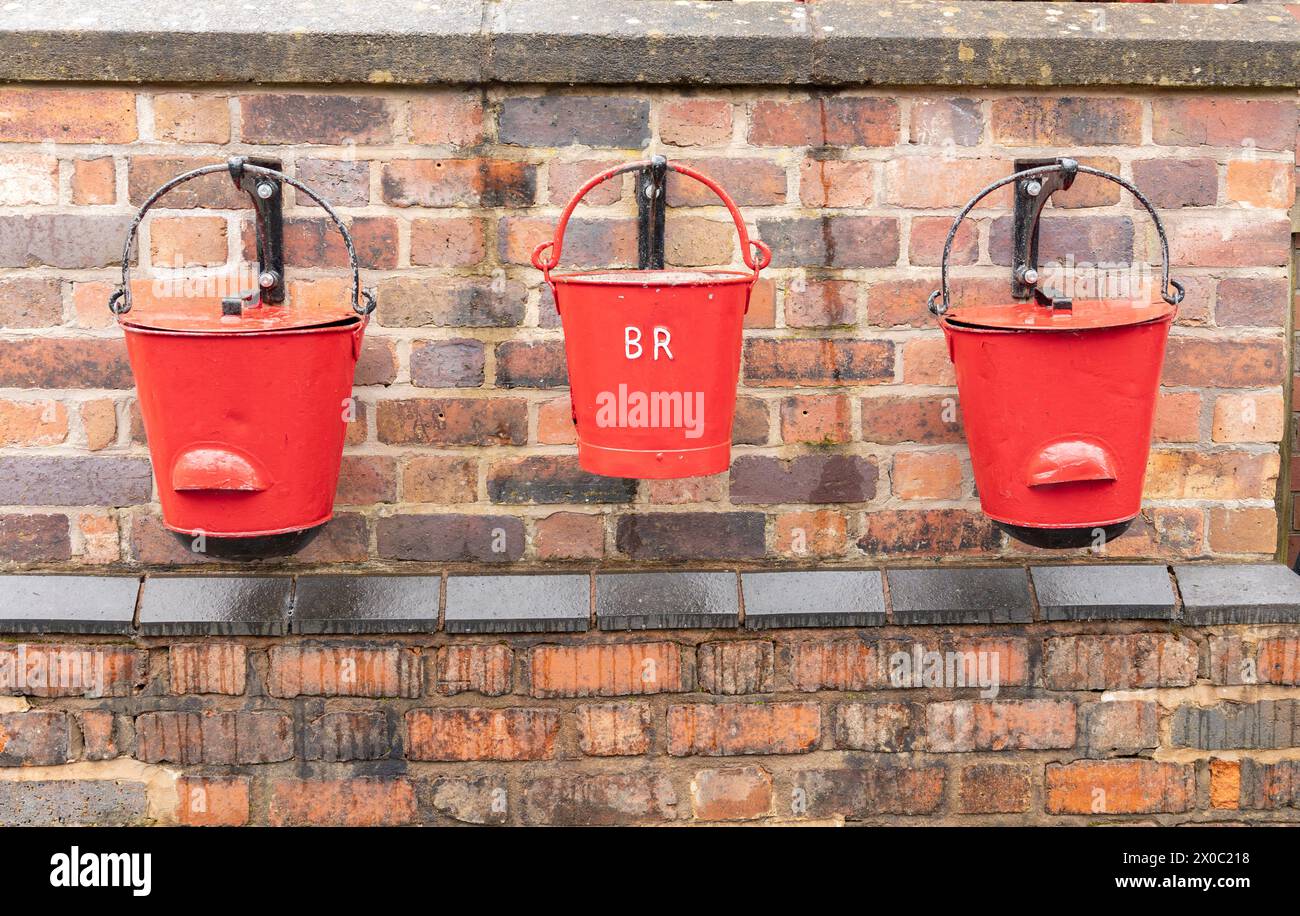 three red fire buckets hanging of a brick wall, used in the past to put ...