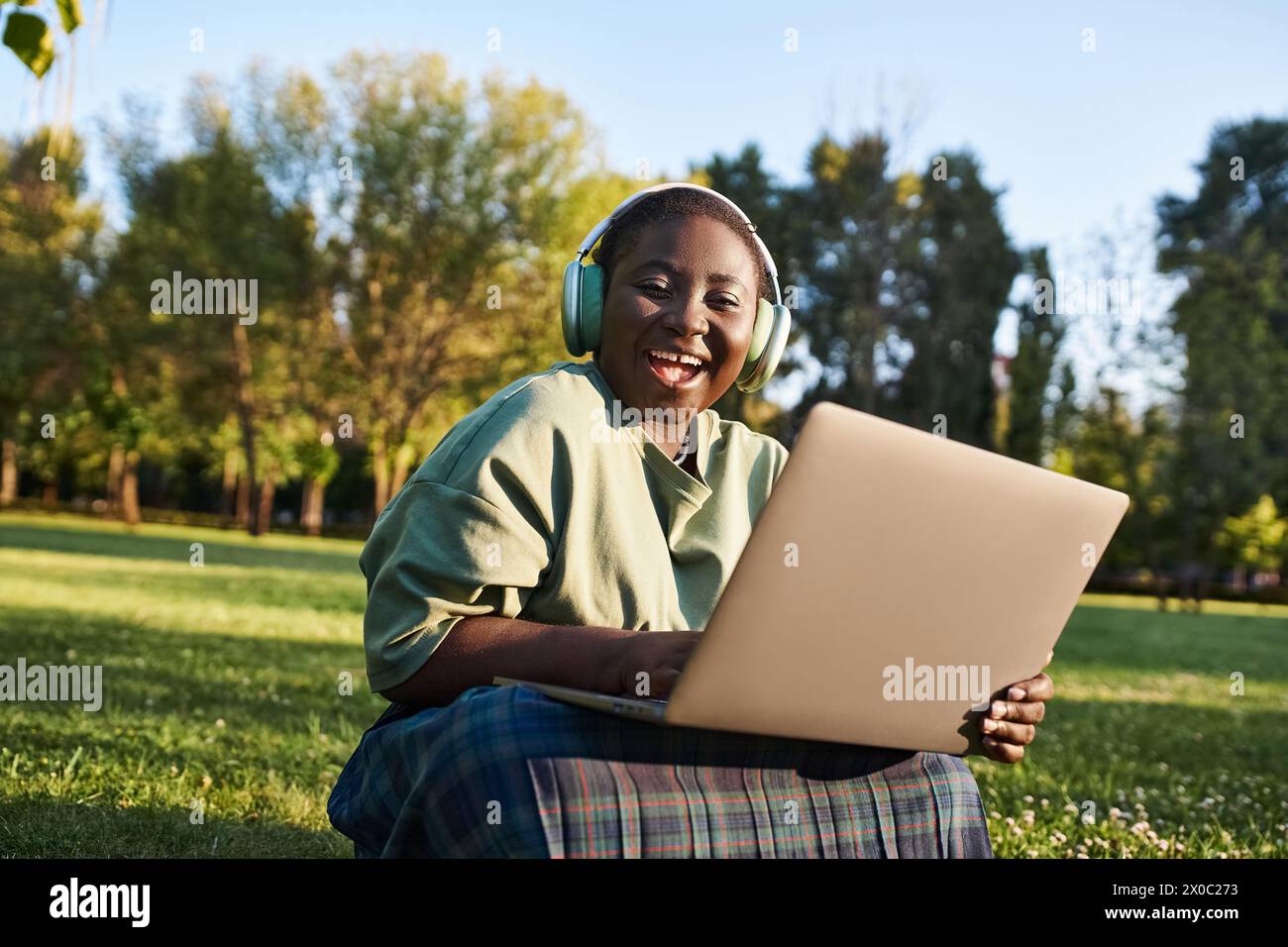 Plus size African American woman sitting in grass with laptop, enjoying ...