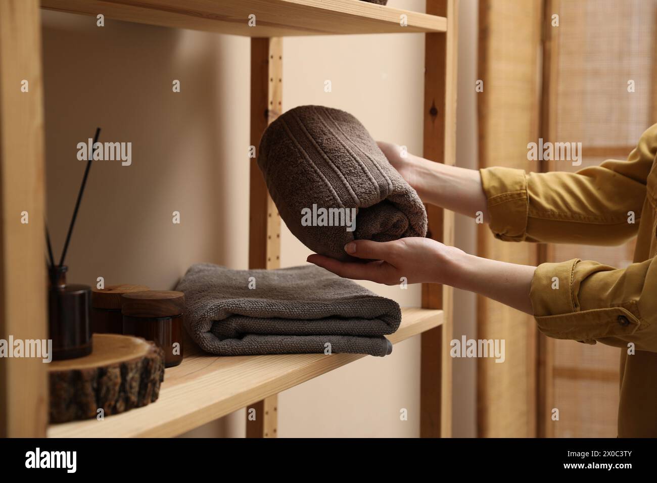 Woman putting rolled towel onto shelf indoors, closeup Stock Photo - Alamy