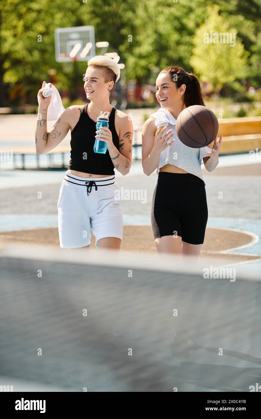 Two athletic young women stand side by side, holding basketballs in an ...