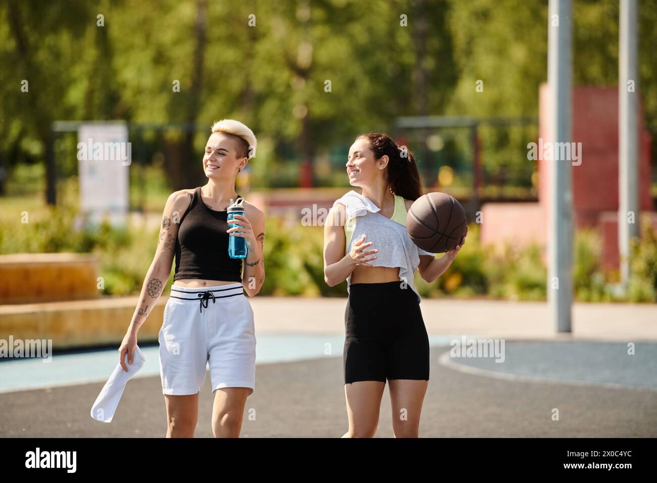Two athletic young women, friends, stand side by side outdoors holding ...