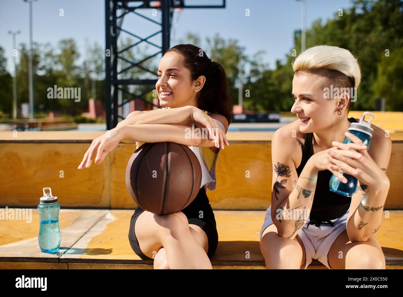 Two young women with a basketball sitting on a bench, engaged in a ...