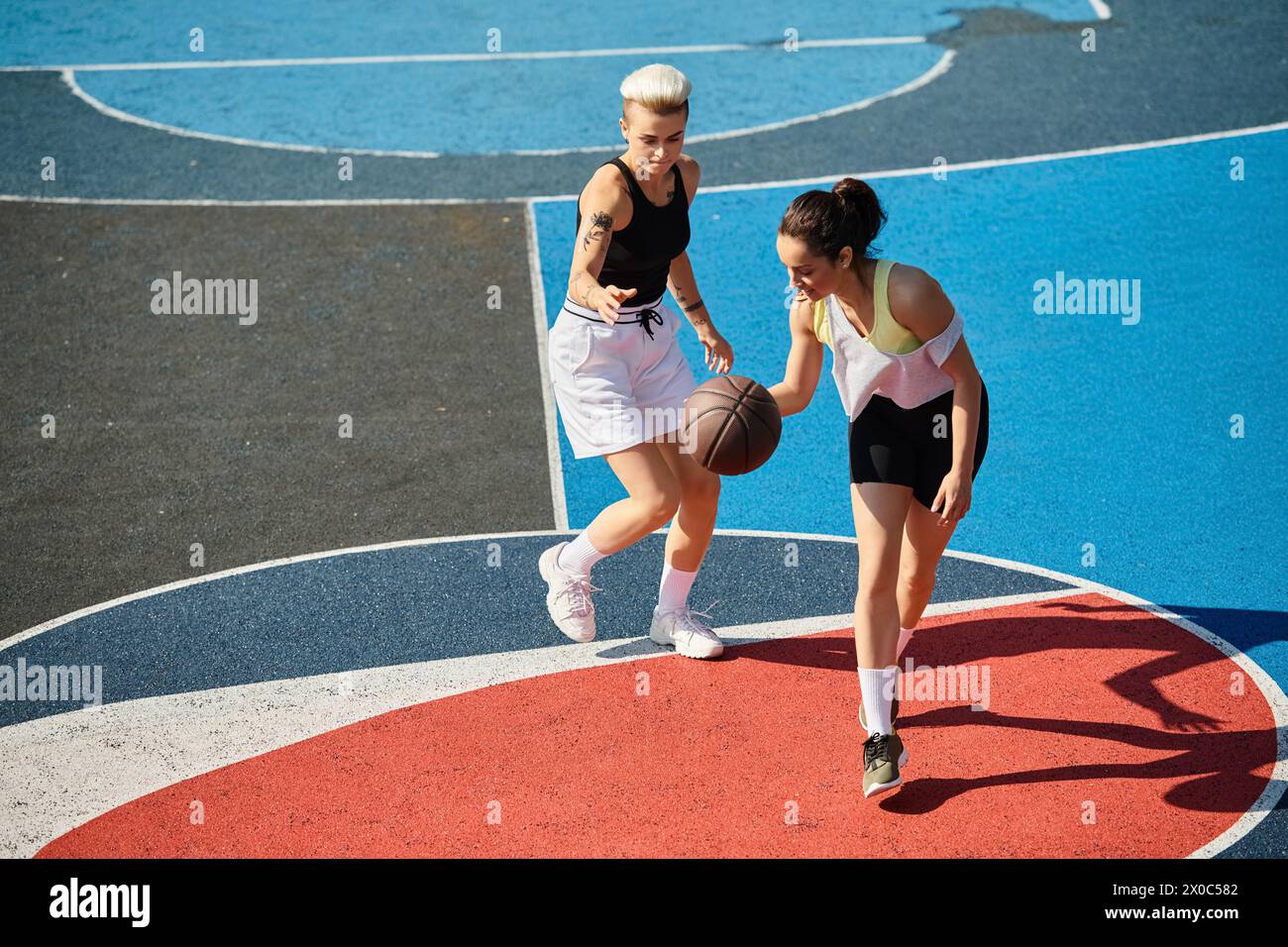 Two young women stand confidently on top of a basketball court, ready to take on the game with ...