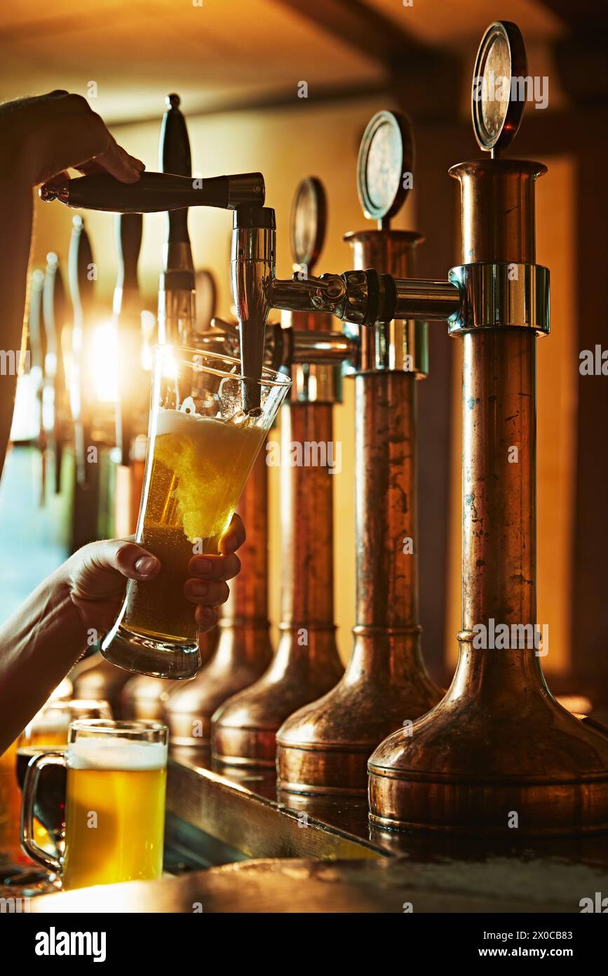 Bartender pouring foamy lager beer into glass from tap, pub interior. Delightful tasting ...