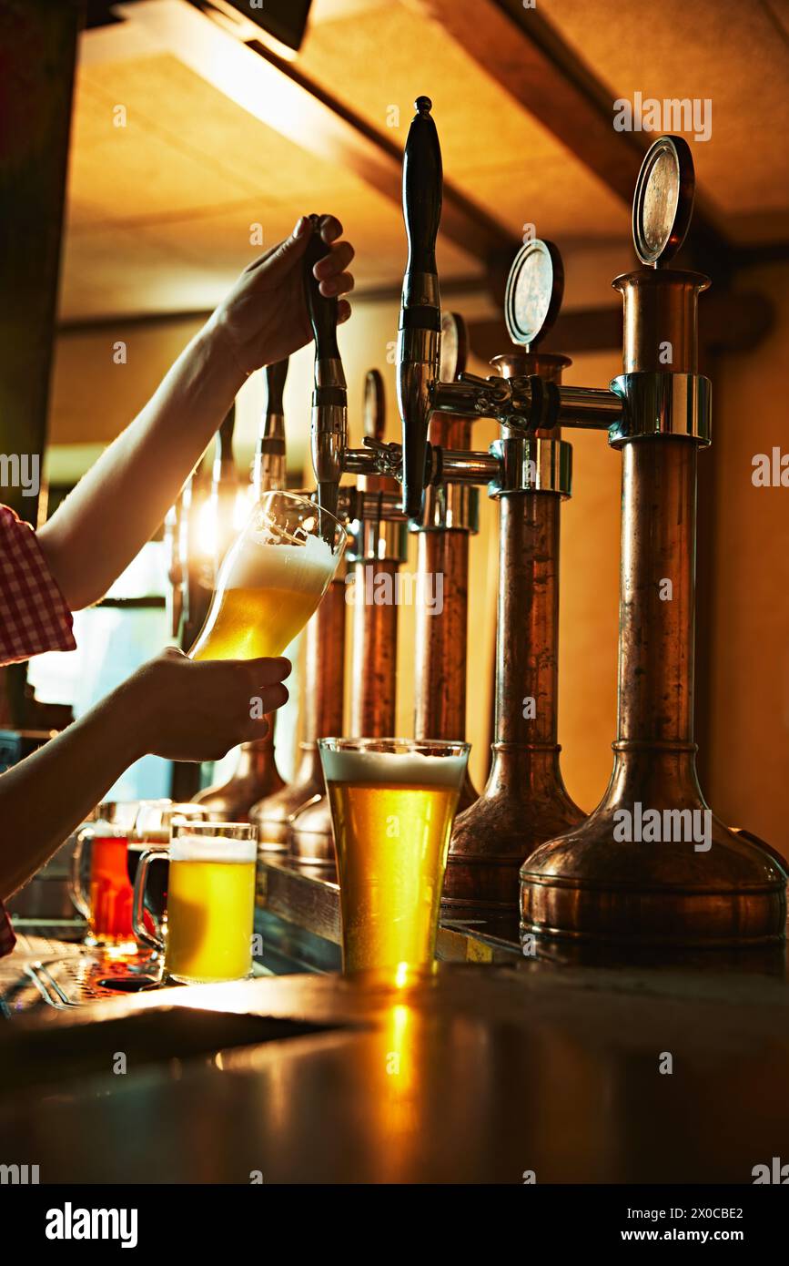Bartender pouring foamy lager beer into glass from tap, pub interior ...