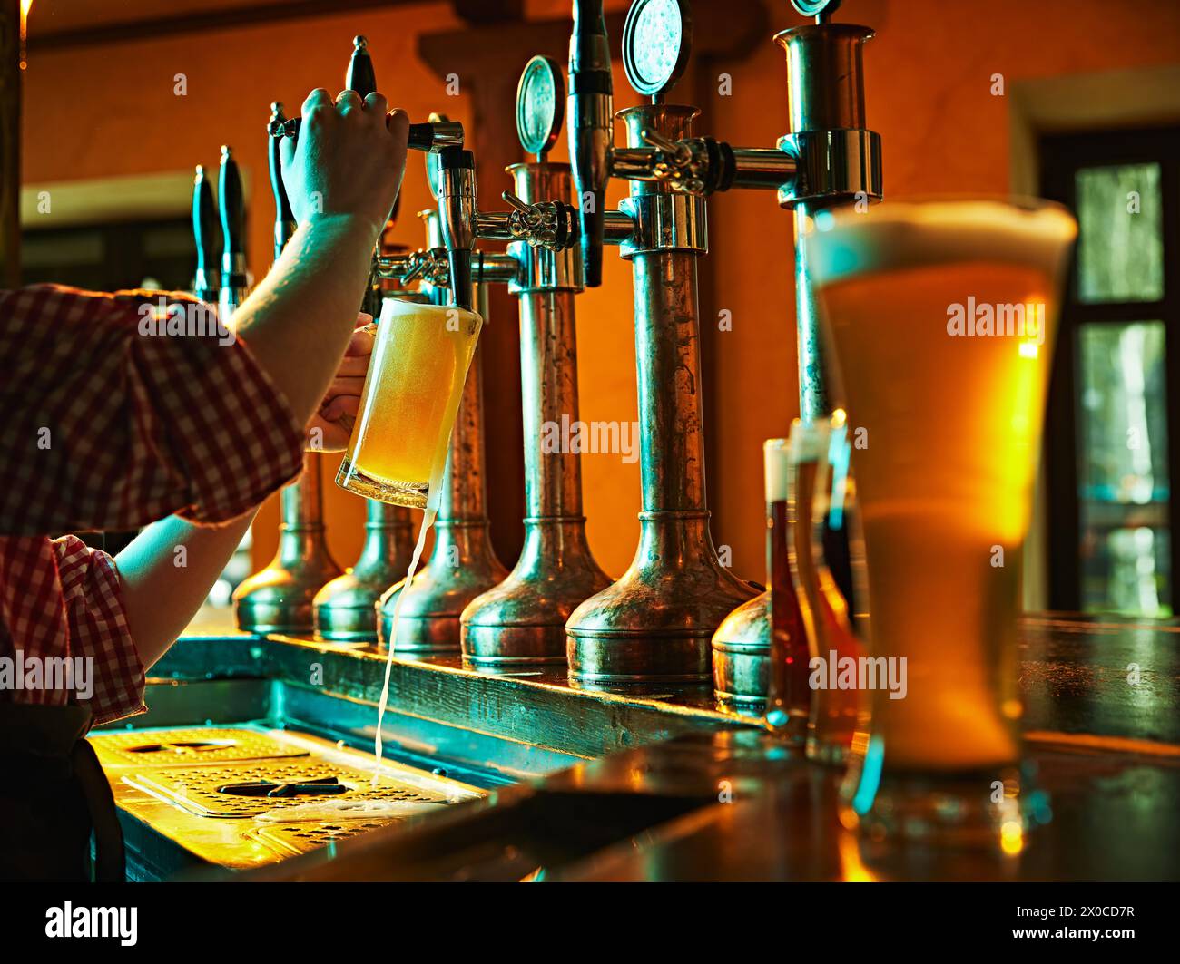 Side view, bartender's hands pouring foamy lager beer from taps in glass. Warm light bar Stock ...