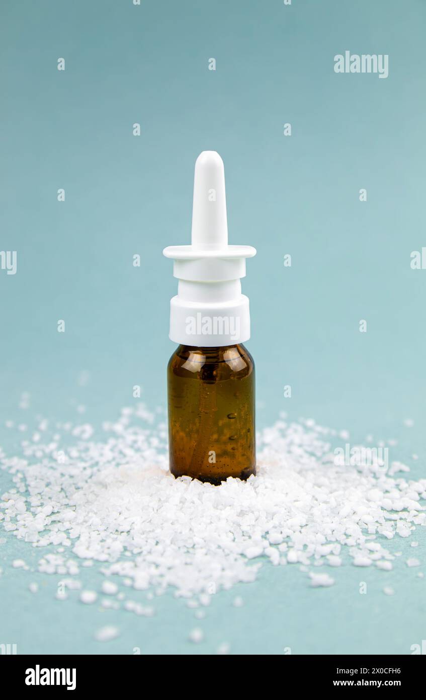 Homemade saline nasal spray bottle on pile of sea salt grains on blue ...