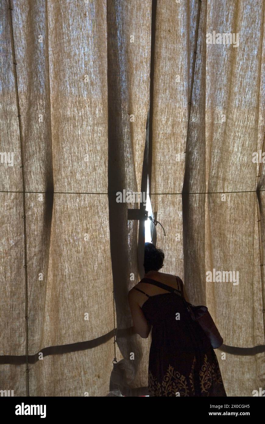 Woman in silhouette looking through a sunscreen curtains, that protects ...