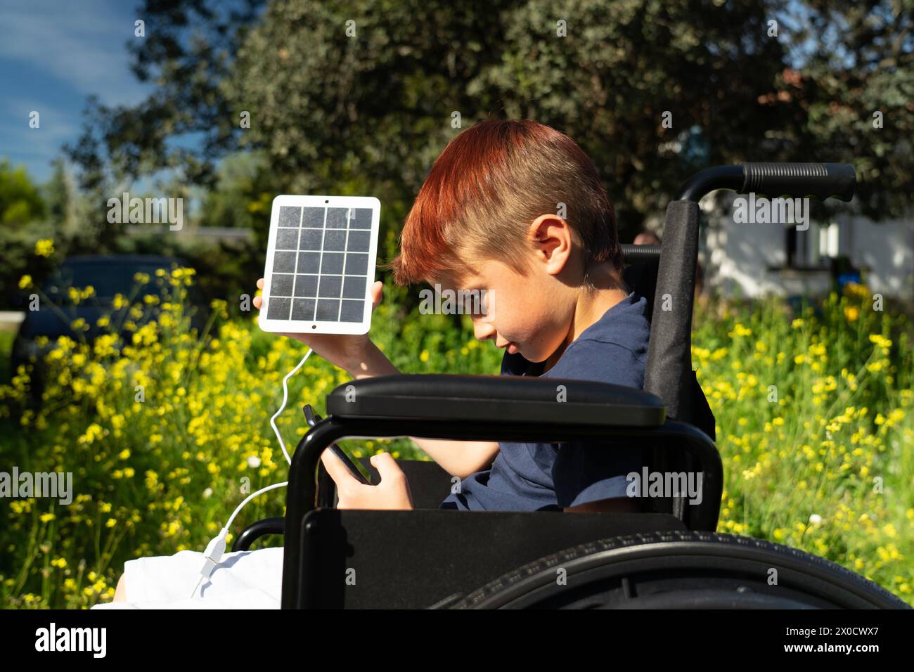 Child in a wheelchair charging a cell phone with a portable solar panel ...