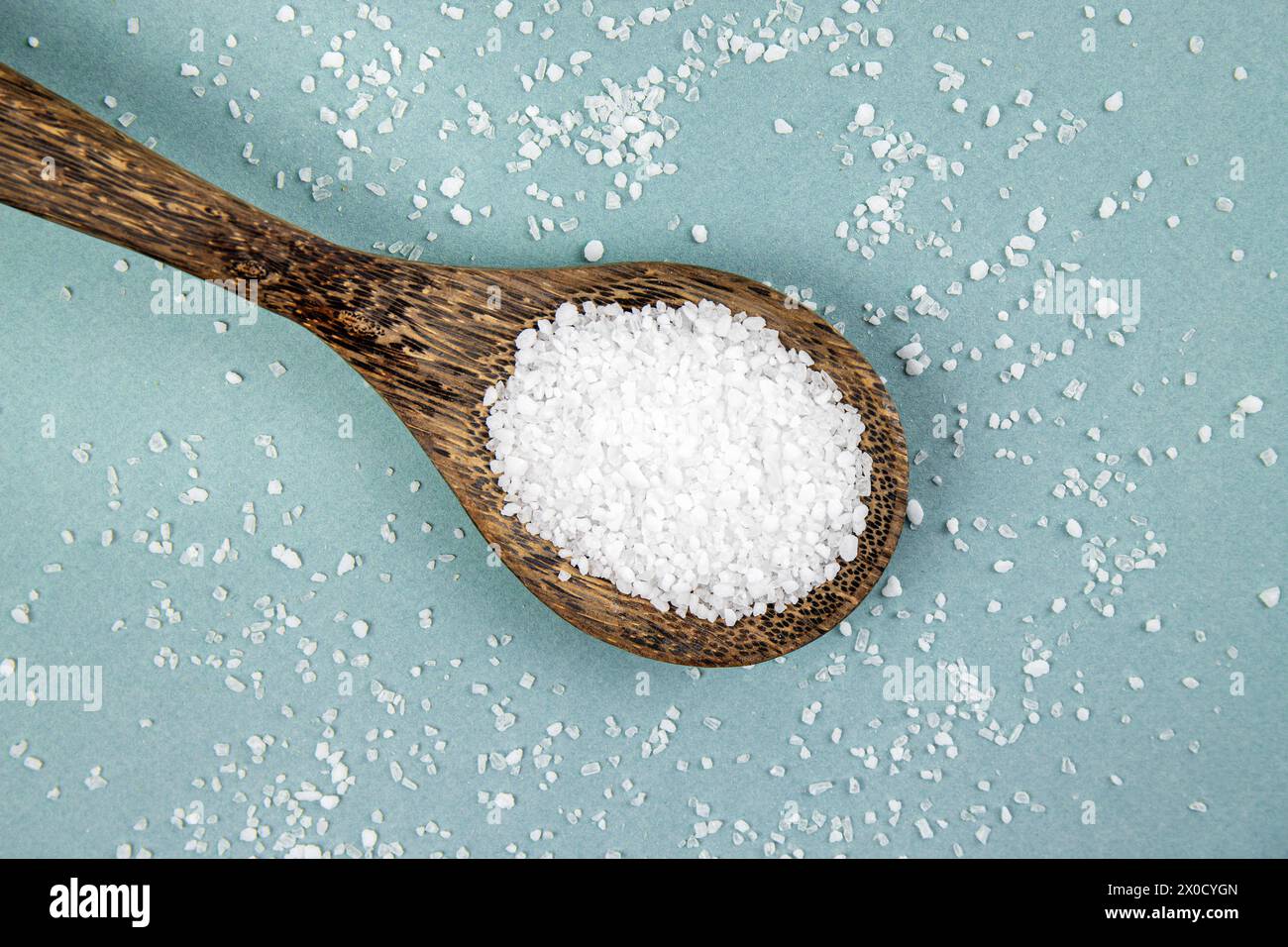 Sea salt grains on wood spoon and scattered around blue background, lot ...