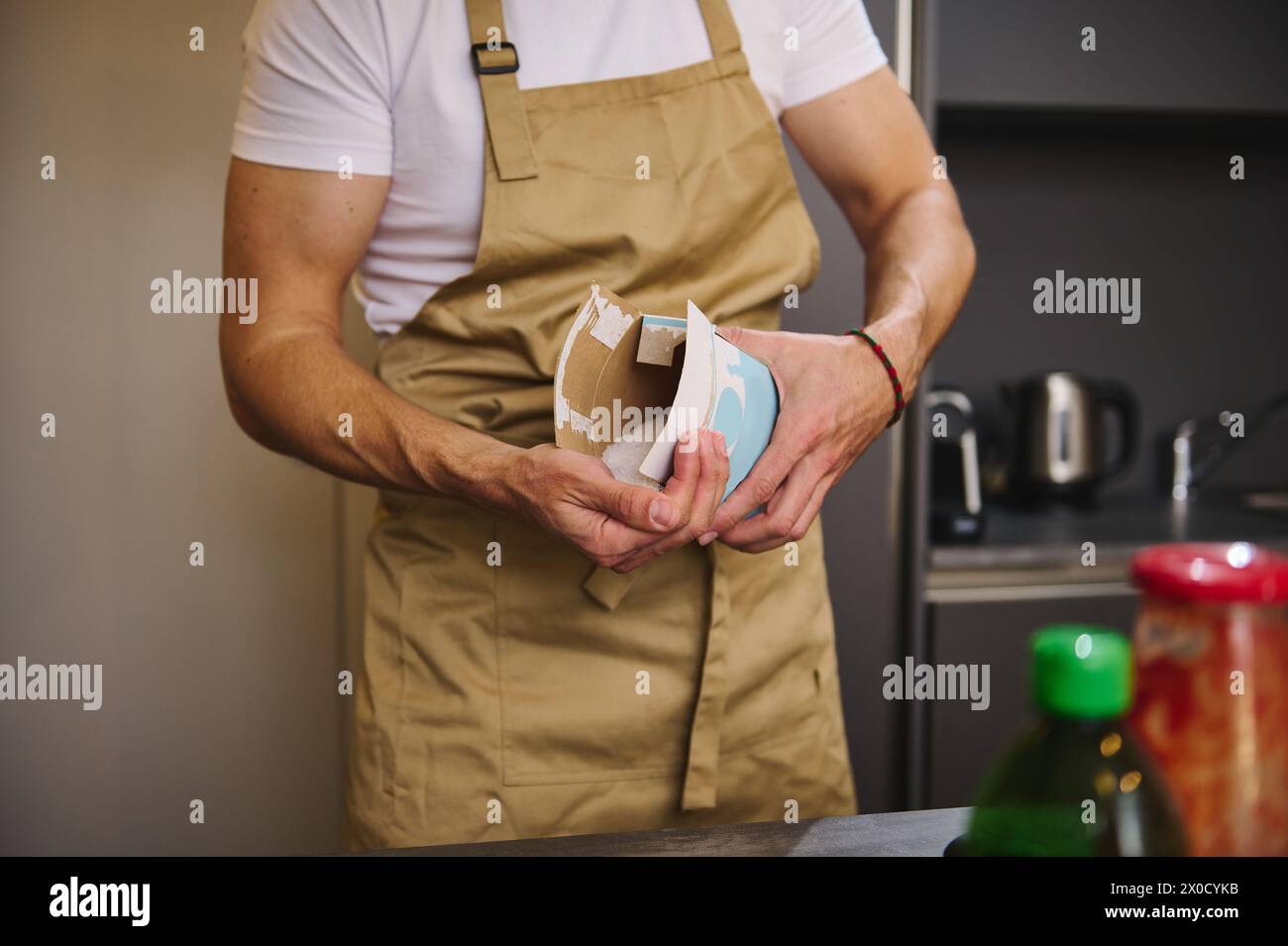 Close-up man chef in beige apron, pouring some salt from paper package ...