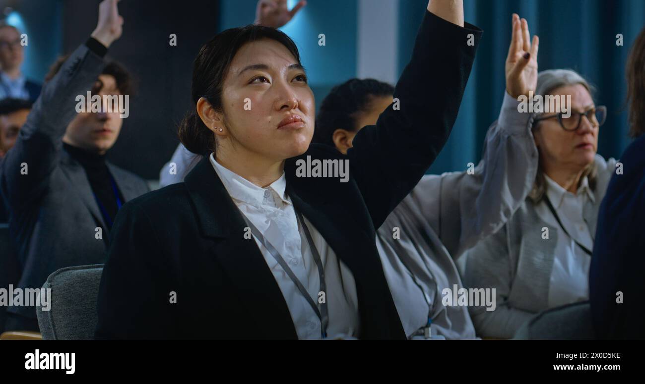 Diverse press workers sit in the conference hall raising hands. Asian ...