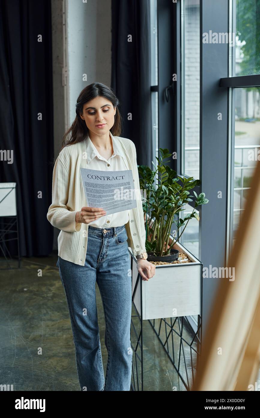 A modern businesswoman reads a contract while standing by a window in ...