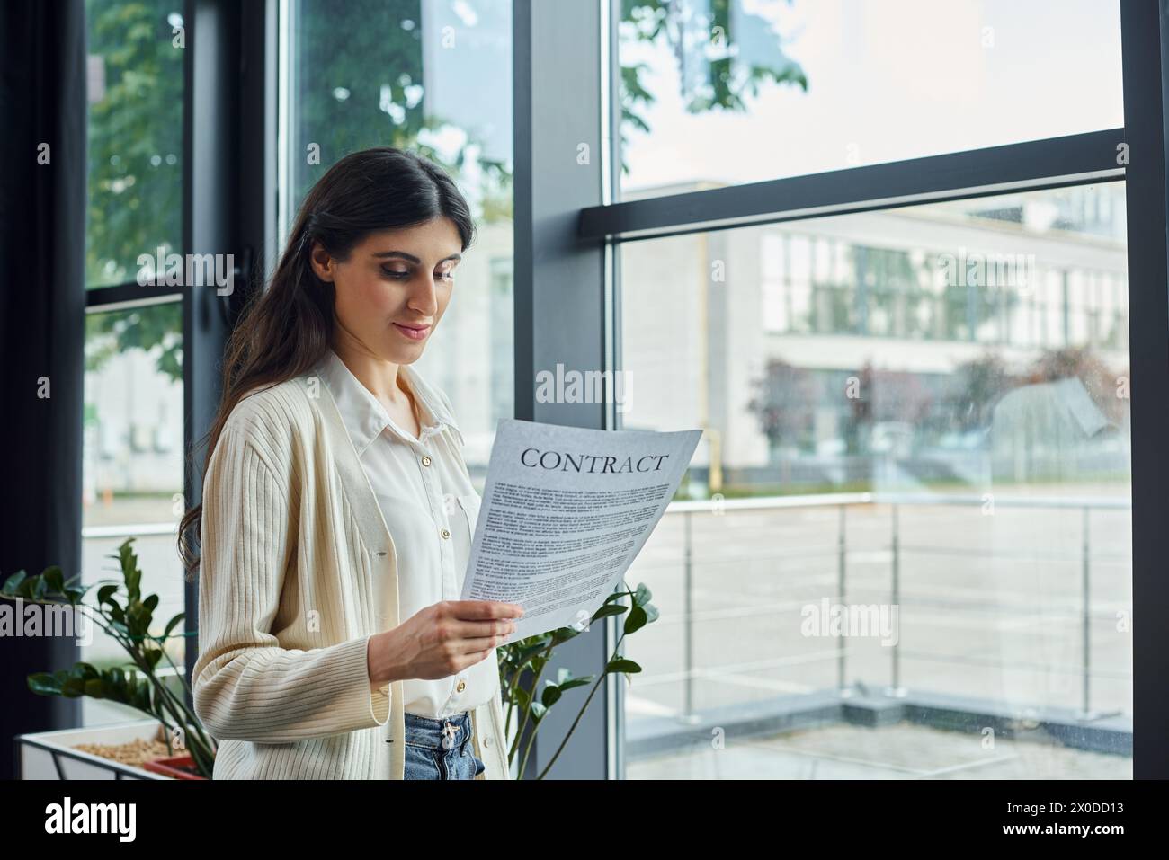A modern businesswoman reads a contract while standing by a window in ...