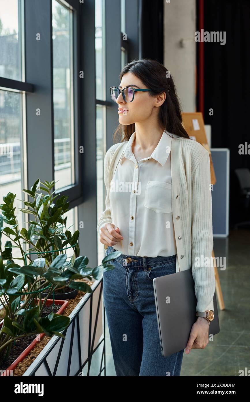 A businesswoman stands by a window, holding a folder in a modern office ...