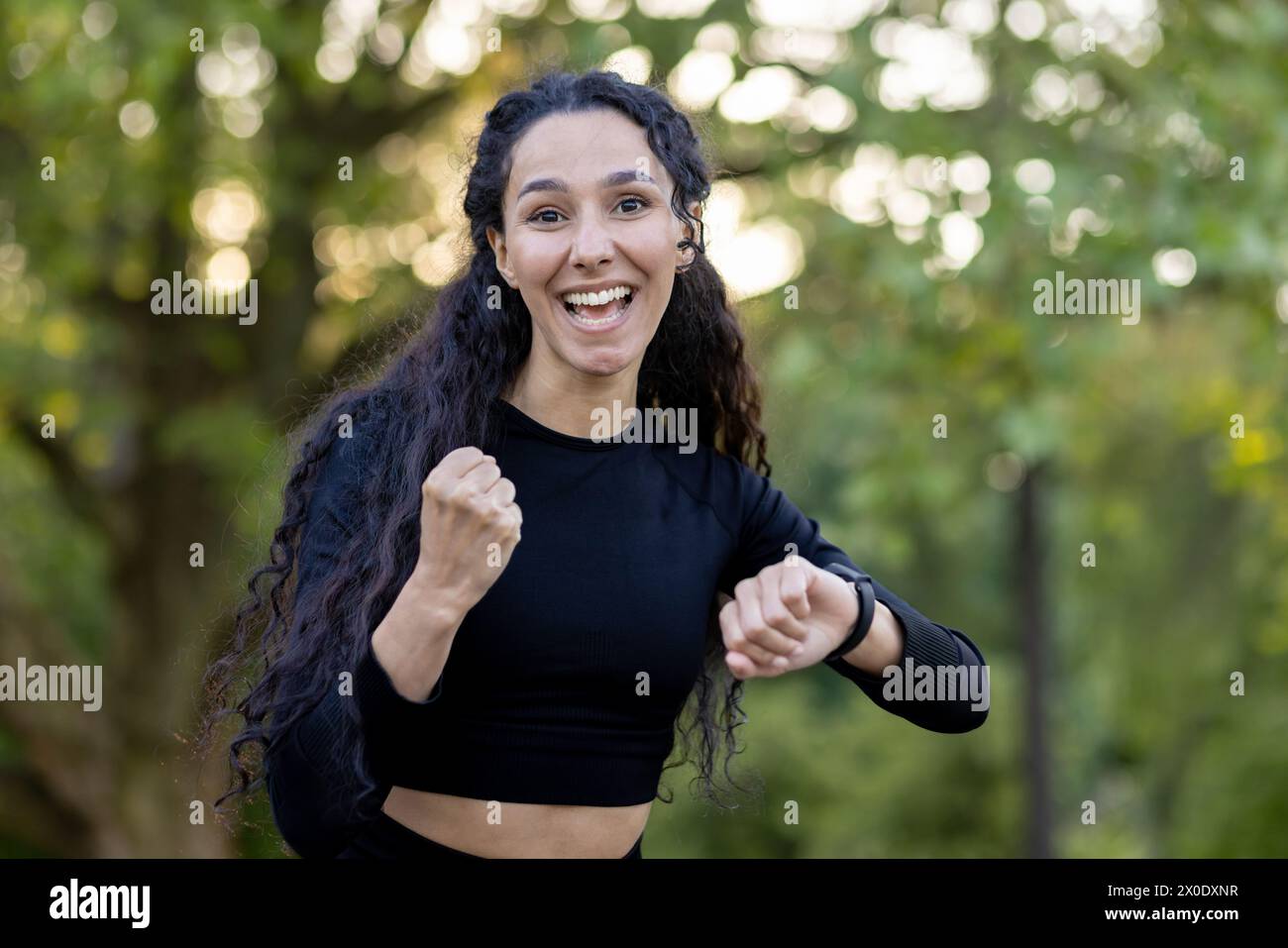 Joyful hispanic woman with fists pumped in victory pose outdoors ...