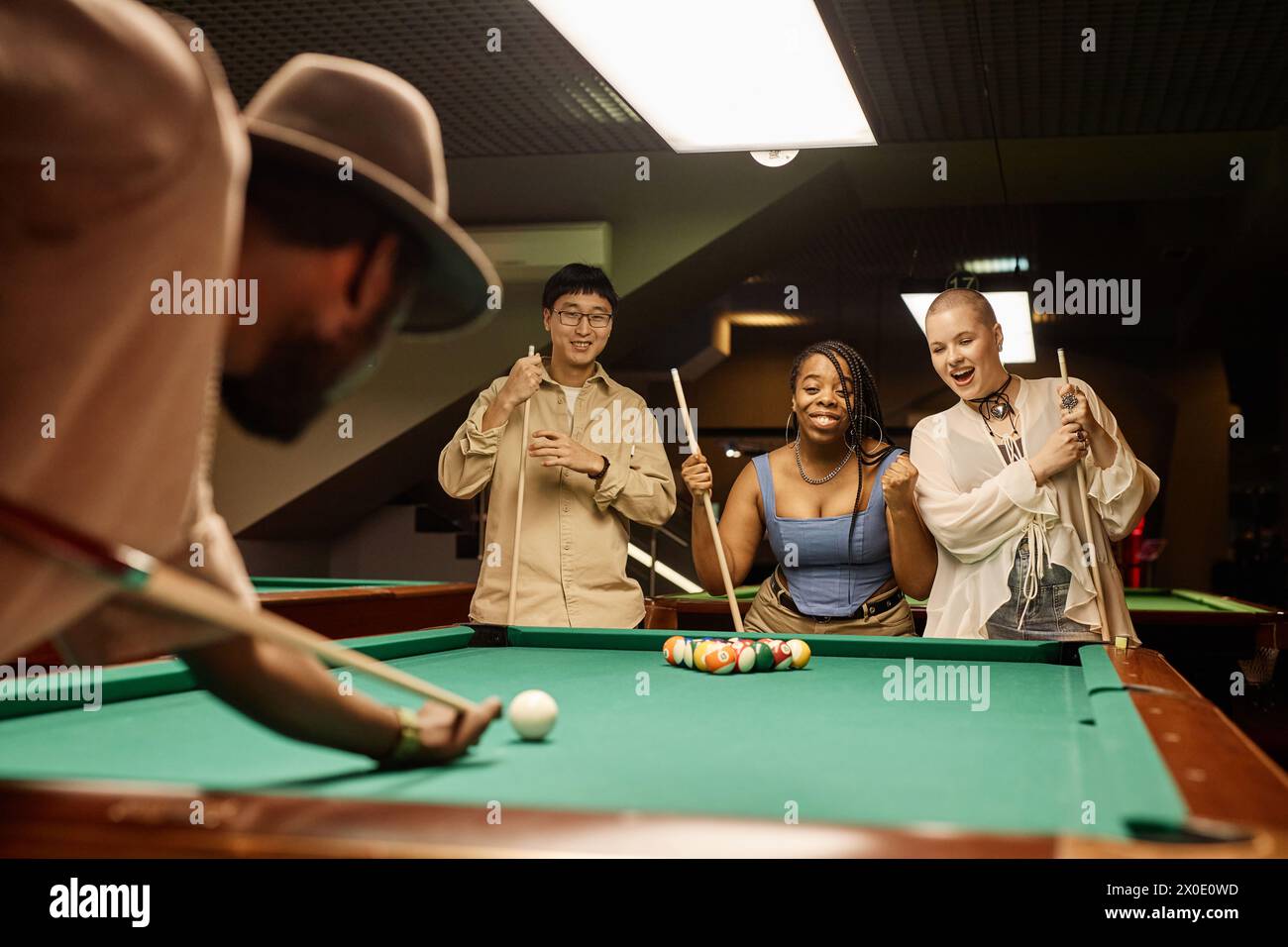 Multiethnic group of emotional people watching friend playing pool and ...