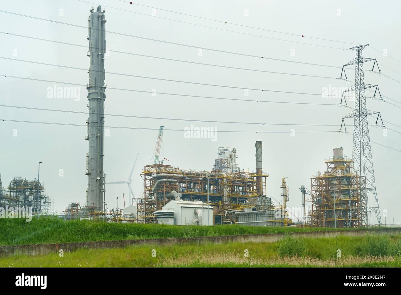 An oil refinery stands tall in the middle of a vast field, with pipes and structures visible ...