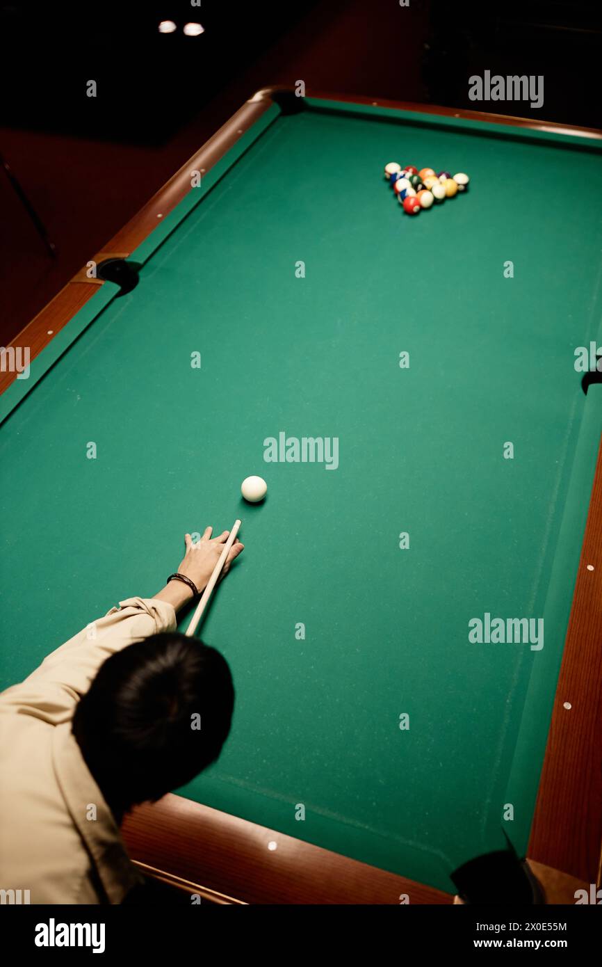 Vertical top view of young man playing pool at table nd hitting ball ...